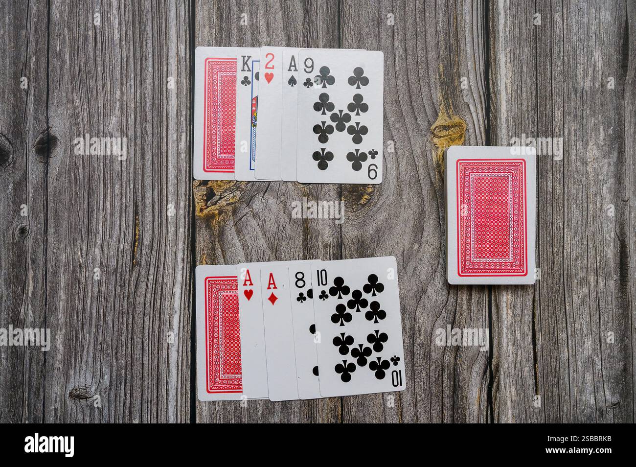 Two hands of playing cards laid out on a rustic wooden surface during a ...