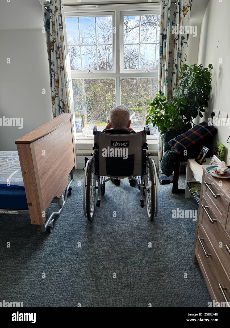 Elderly man in a wheelchair looking out of the window of a care home ...