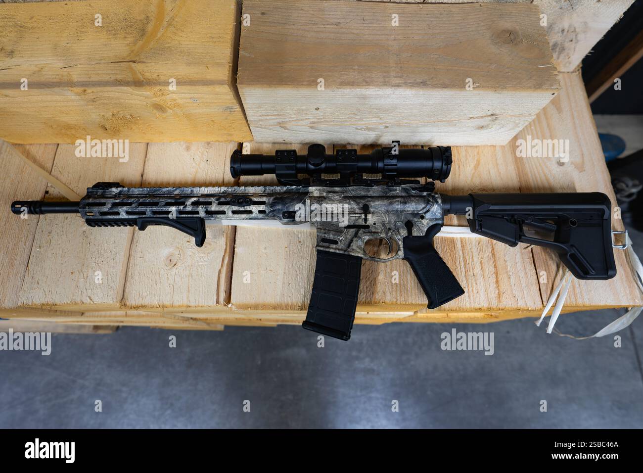 A tactical marksman rifle with an optical sight lies on wooden pallets ...