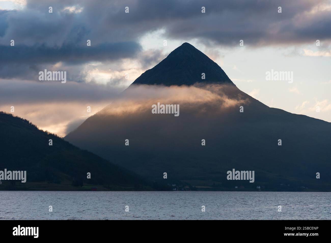 Pyramid shaped mountain in northern Norway with glowing clouds passing ...