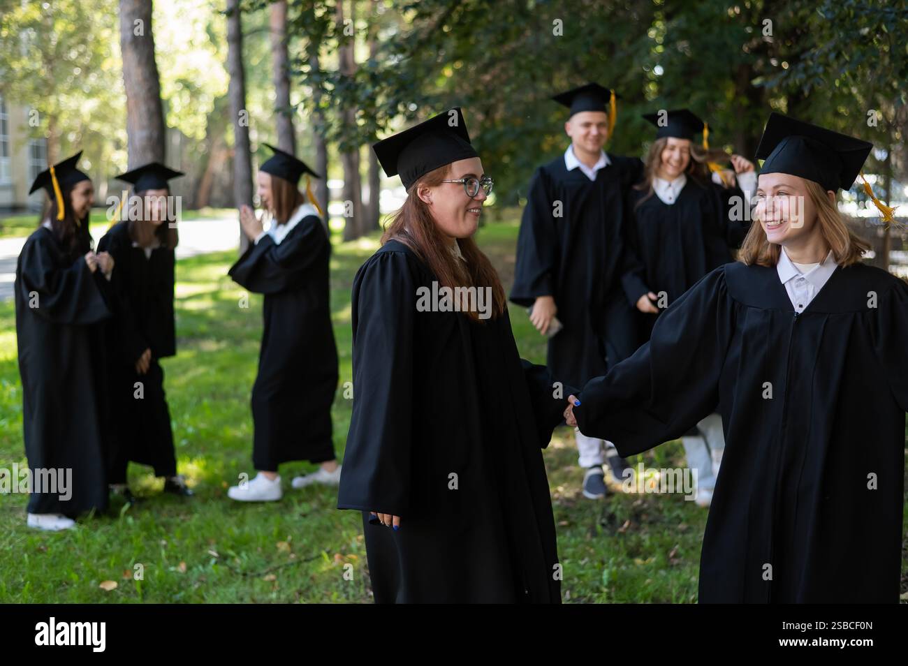 Group of happy students in graduation gowns outdoors. In the foreground ...