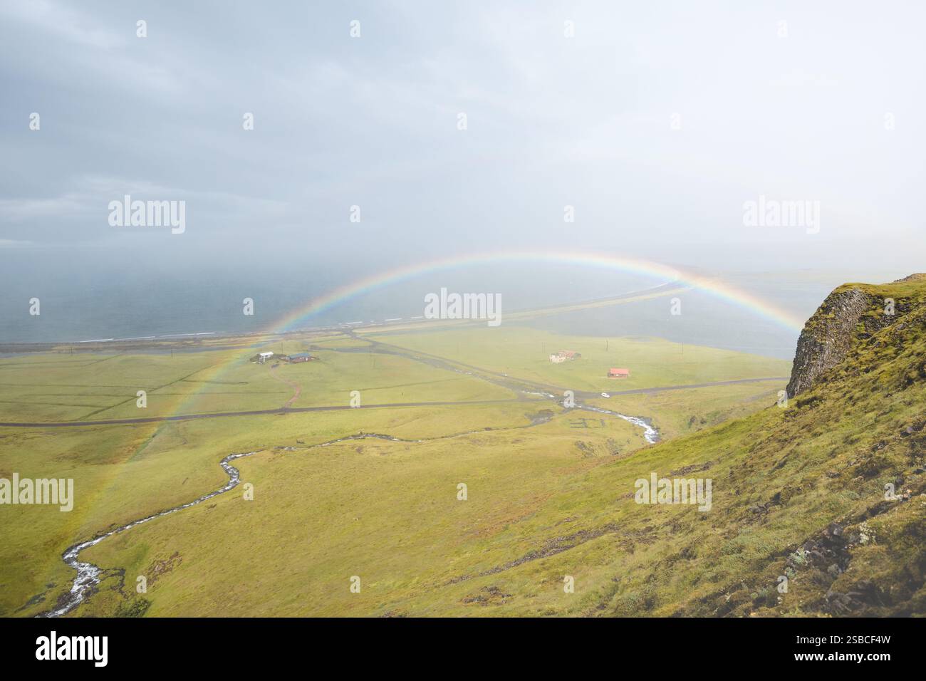 Vivid rainbow stretches across the cloudy sky above a serene Icelandic ...