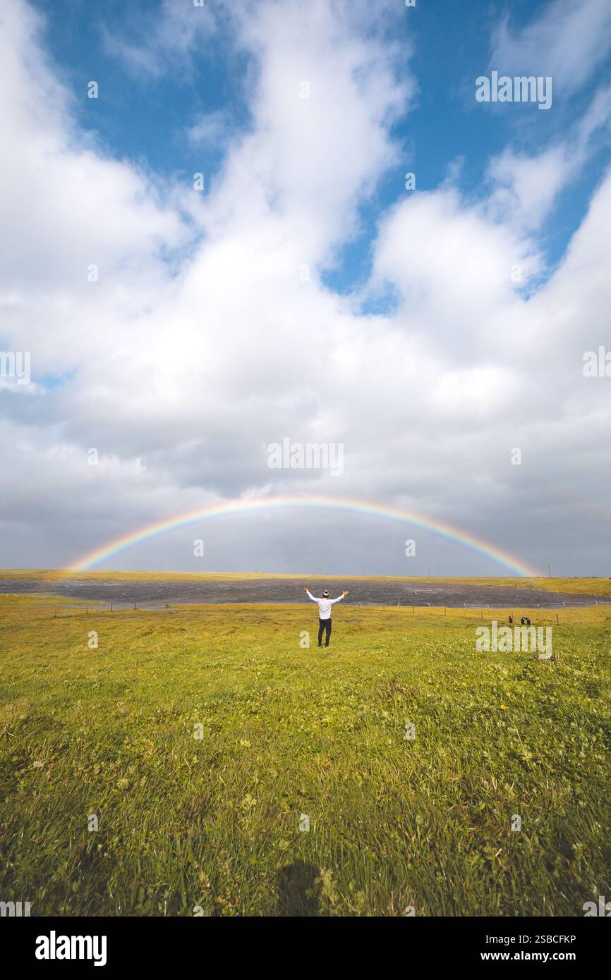 Person stands with arms wide open on a lush green meadow under a ...