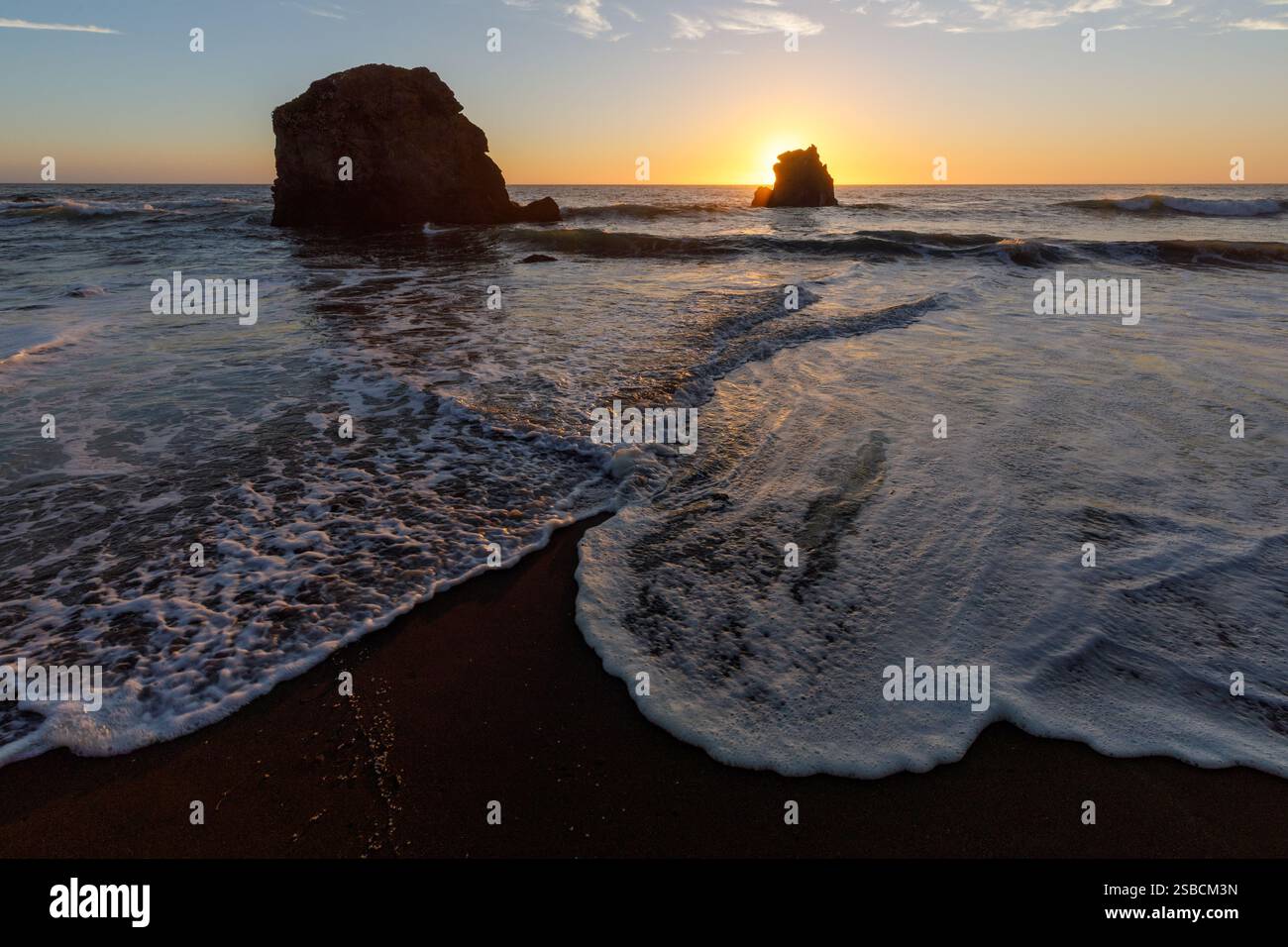 waves spread across the sand at sunset on rocky coastline beach Stock ...
