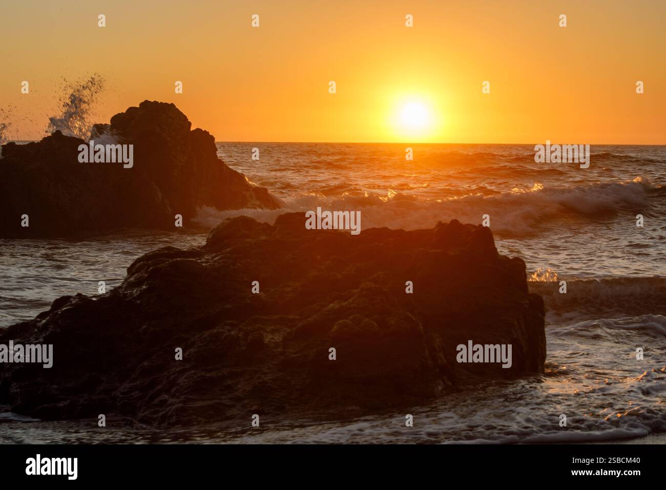 Orange glowing sunset on rocky coastline beach Stock Photo - Alamy