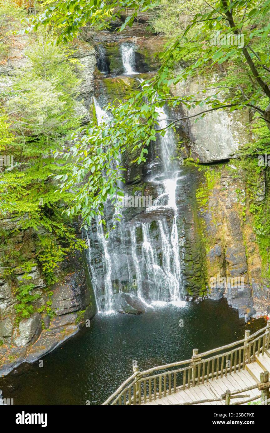 Water cascades down a rocky cliff into a tranquil pool, with visitors ...