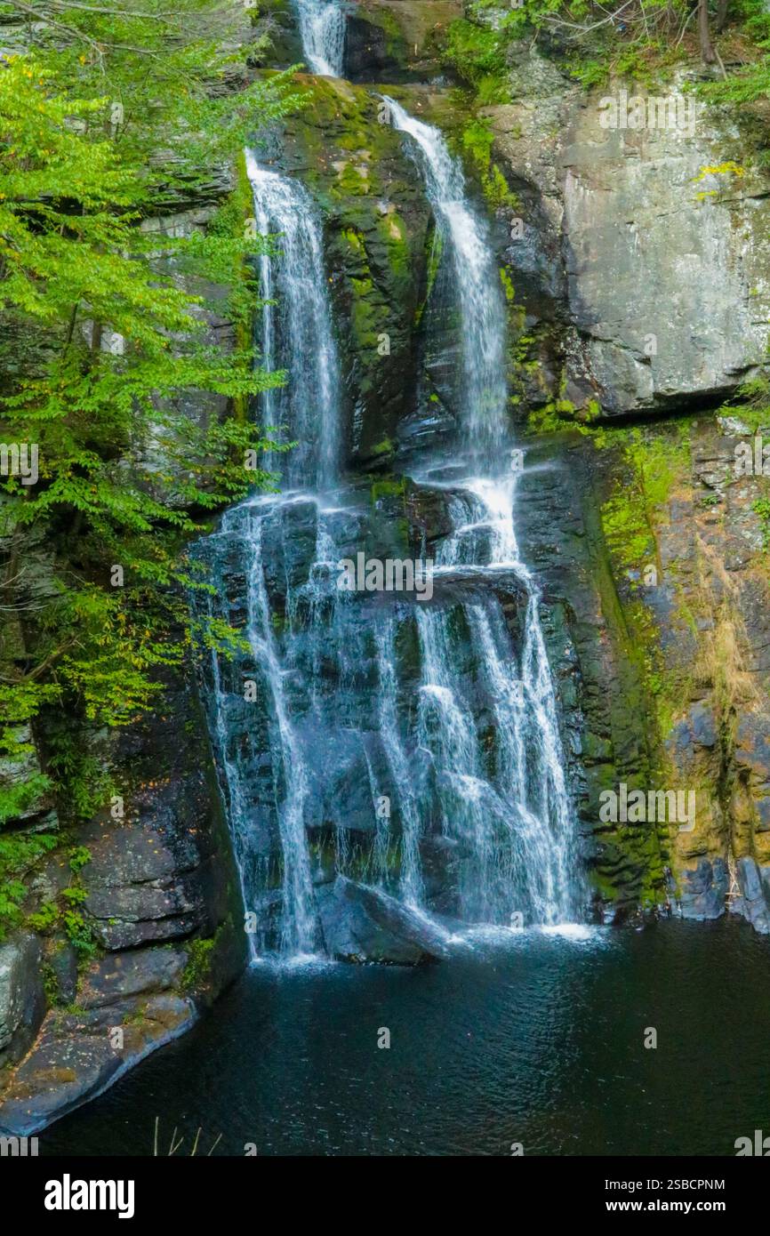 Water cascades down a rocky cliff into a tranquil pool, with visitors ...