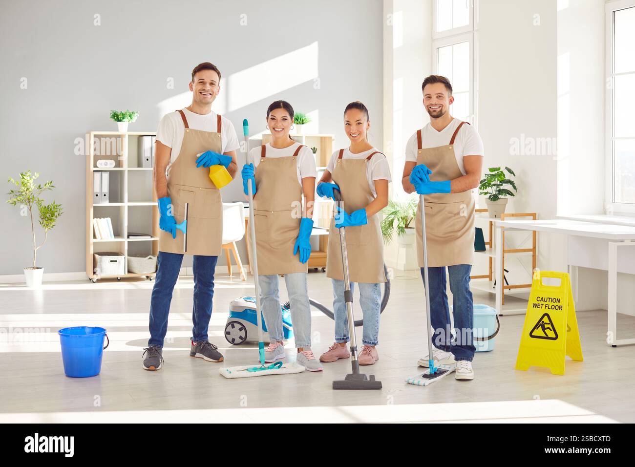 Happy janitors in uniform from professional cleaning service looking at ...