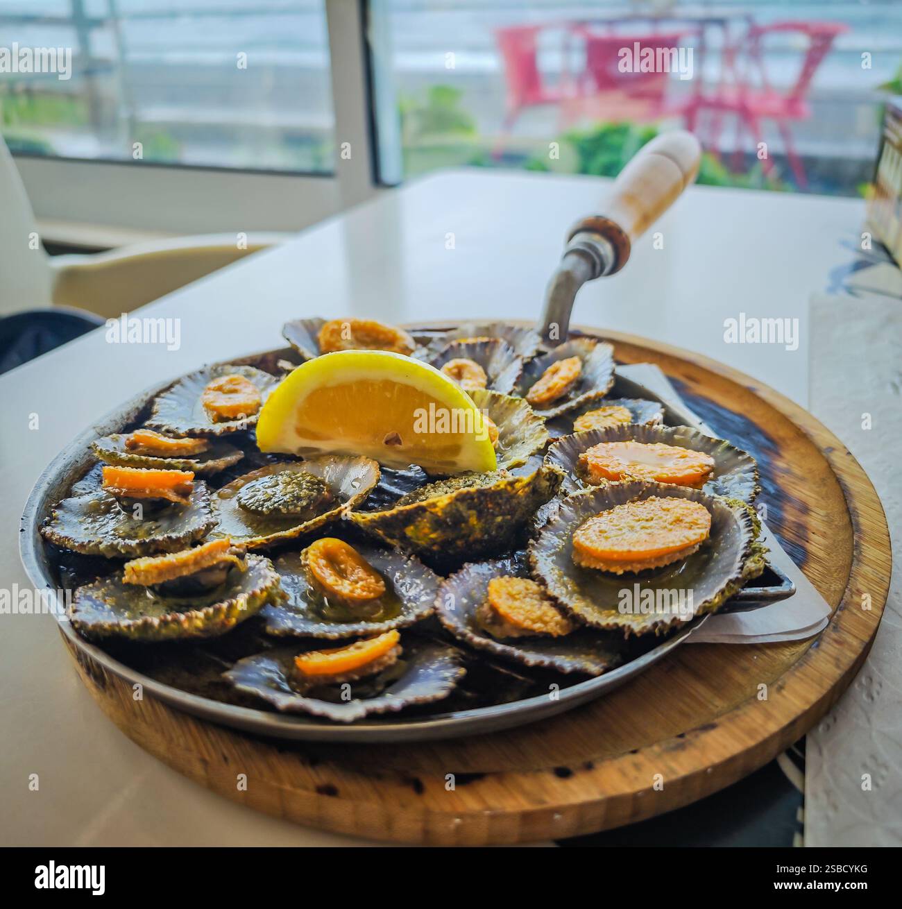 Grilled limpets served on a cast iron with a lemon slices in a ...