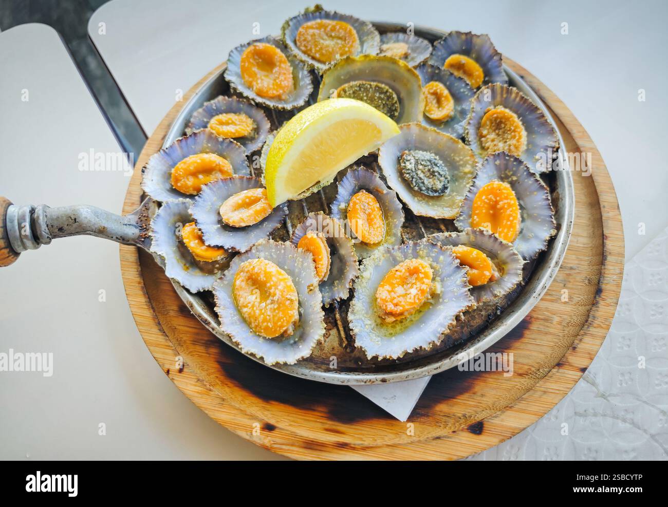 Grilled limpets served on a cast iron with a lemon slices in a ...