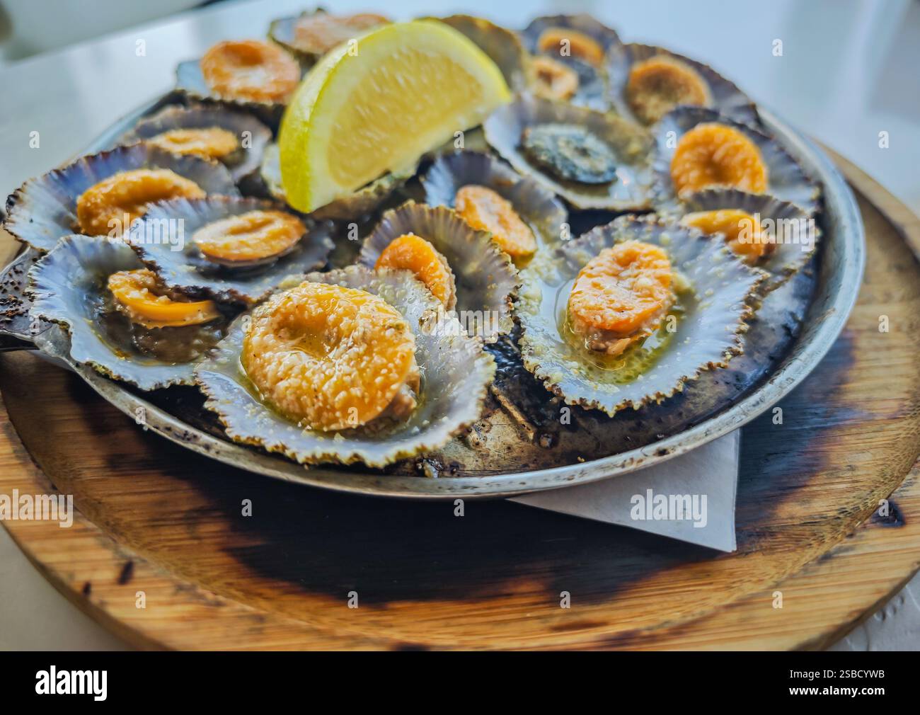 Grilled limpets served on a cast iron with a lemon slices in a ...
