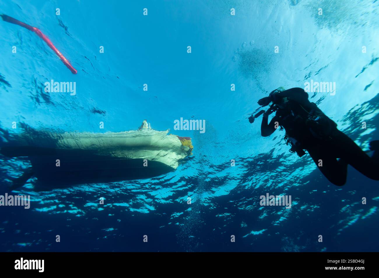 Scuba diver ascending and aproaches dive boat from below in clear blue ...