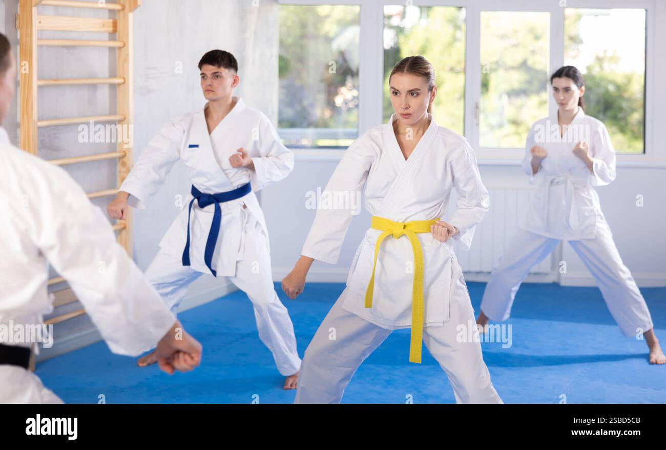 Young woman attendee of karate classes practicing kata standing in row ...