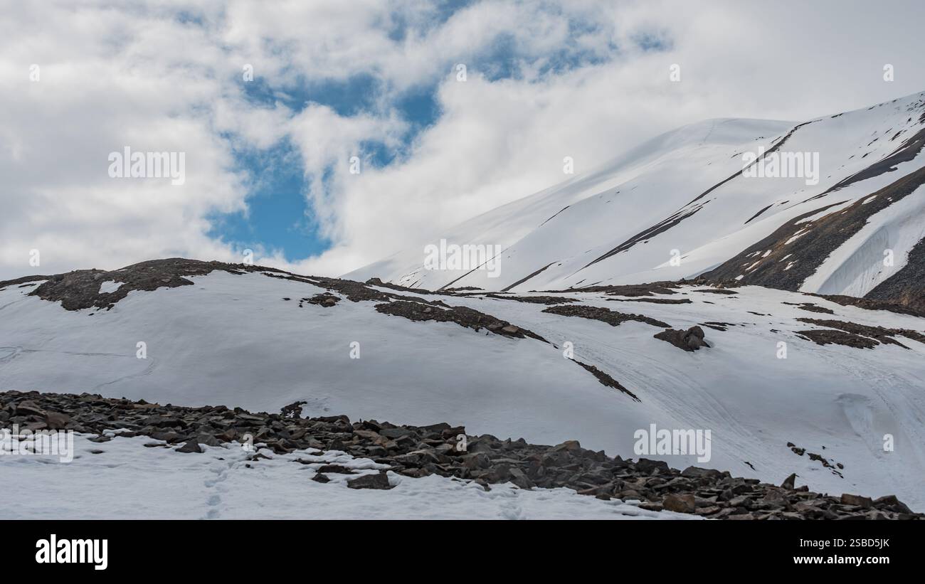 Rocky patches on the side of a snowy mountain with tracks in Svalbard ...