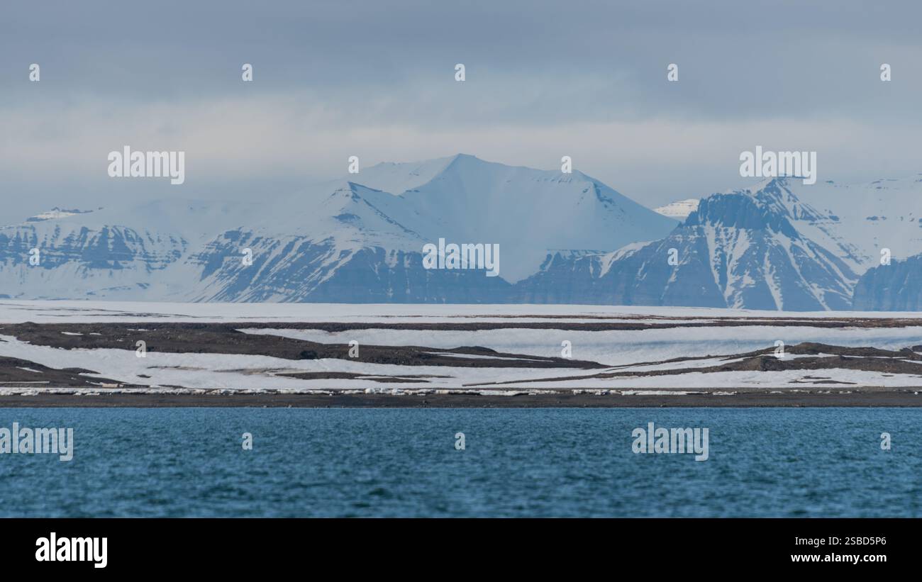 Landscape of distant snow covered mountains behind the rocky shore of ...