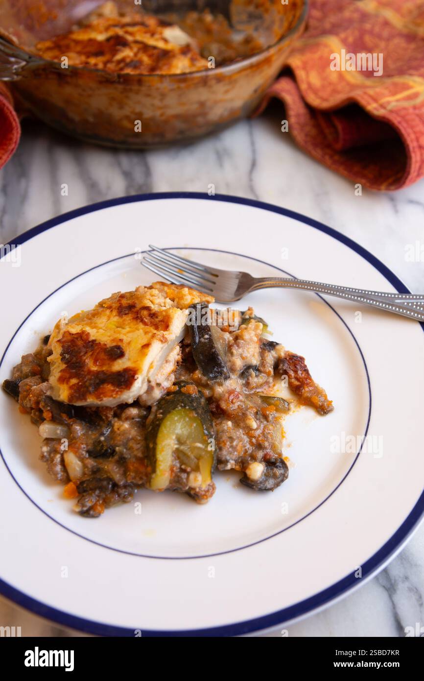 A serving of Homemade greek moussaka on a plate with cooked moussaka in ...
