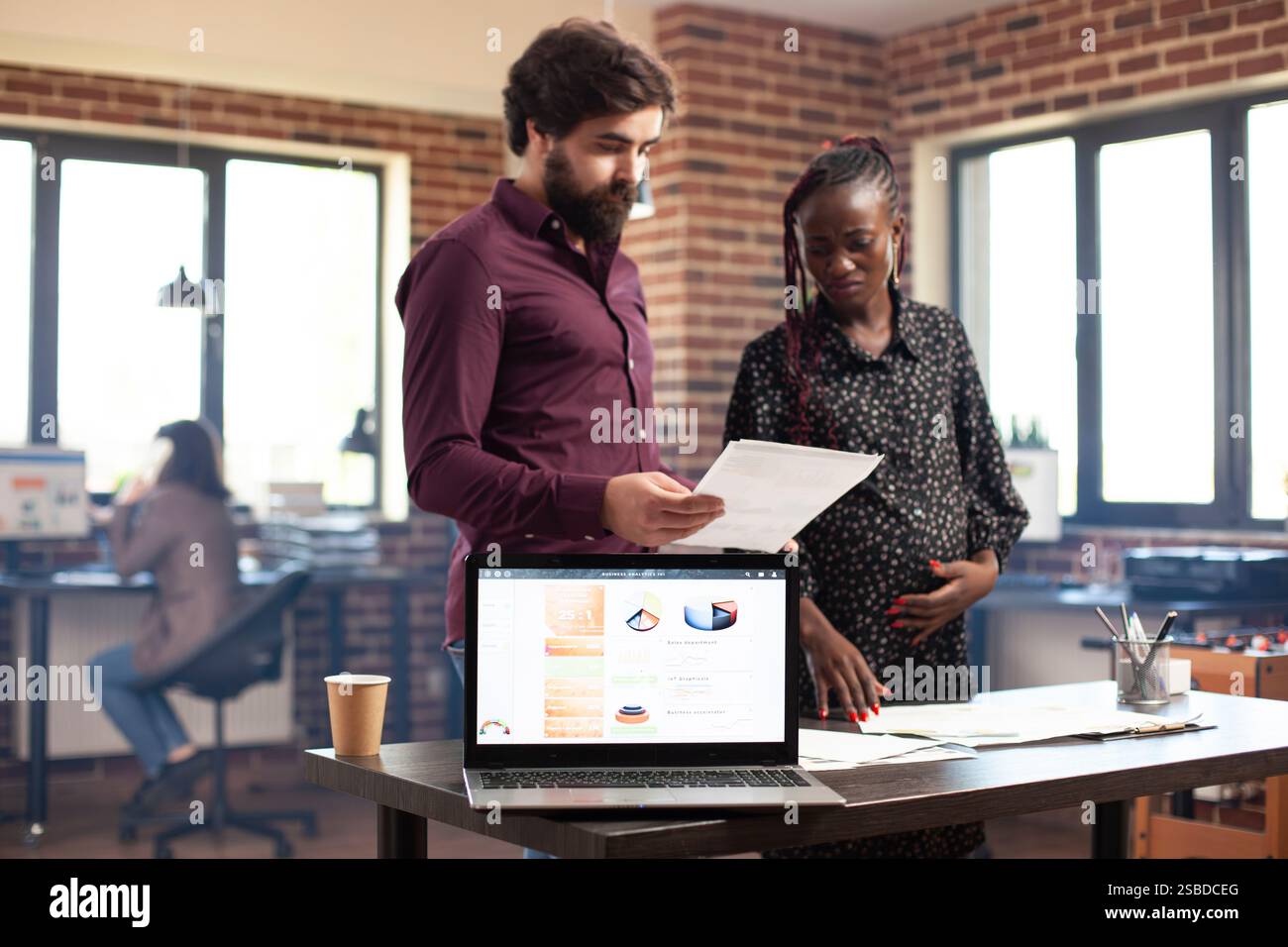 Black expectant mother discussing with male colleague as financial ...