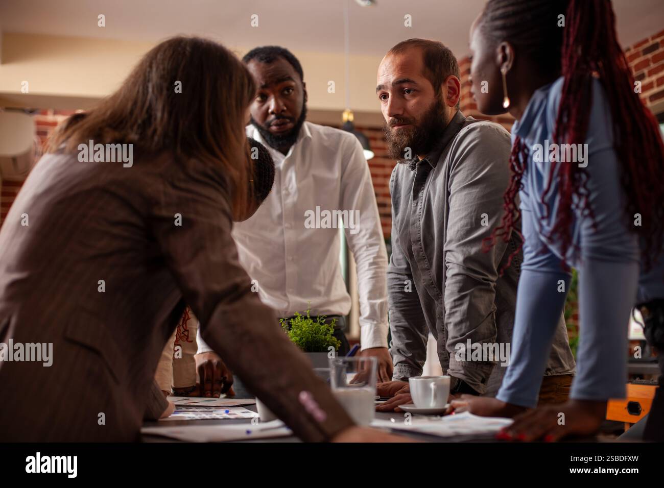 Closeup of multiethnic coworkers standing around table and having ...