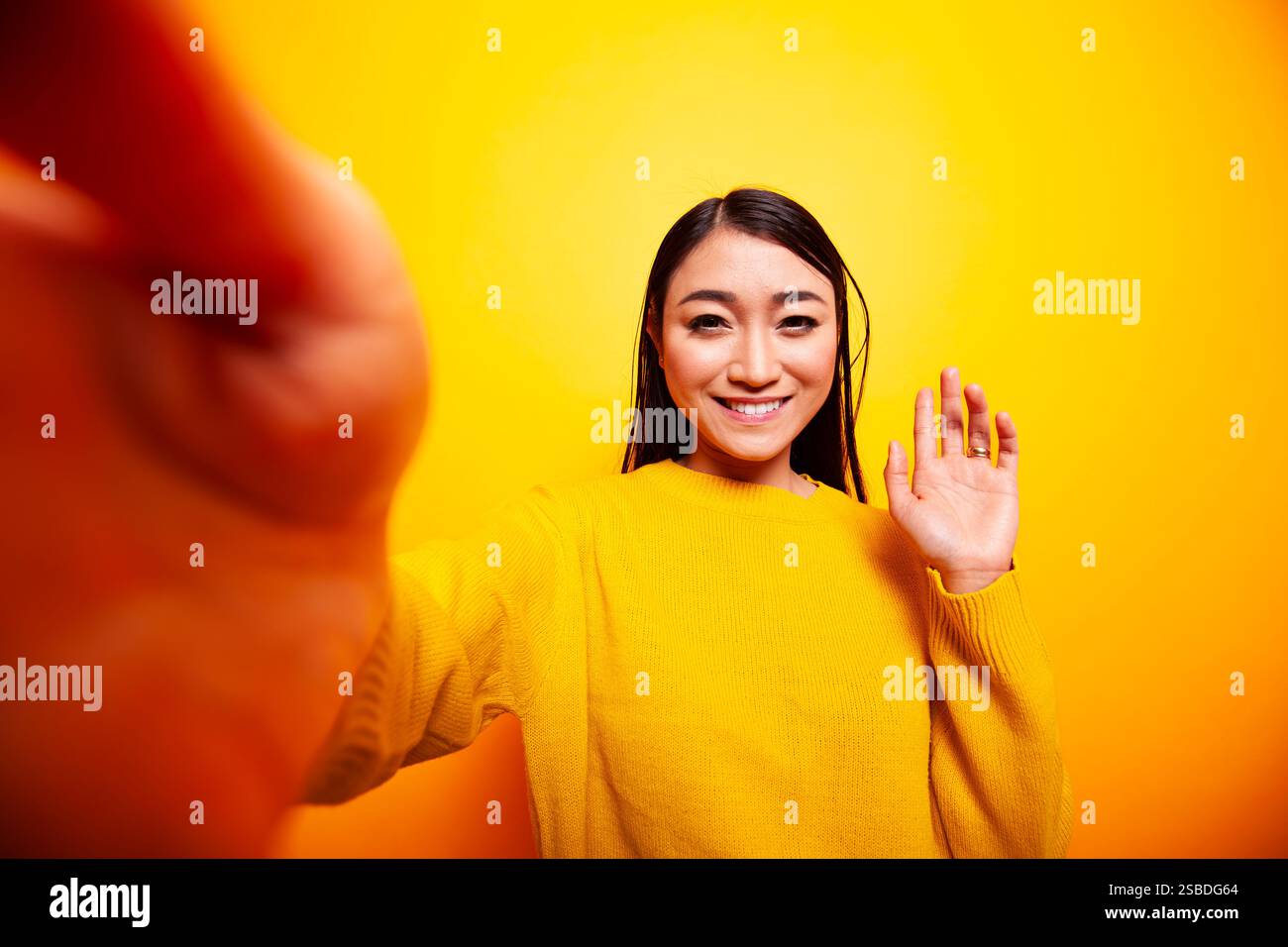Smiling asian lady making a hello gesture towards the camera, vlogging ...
