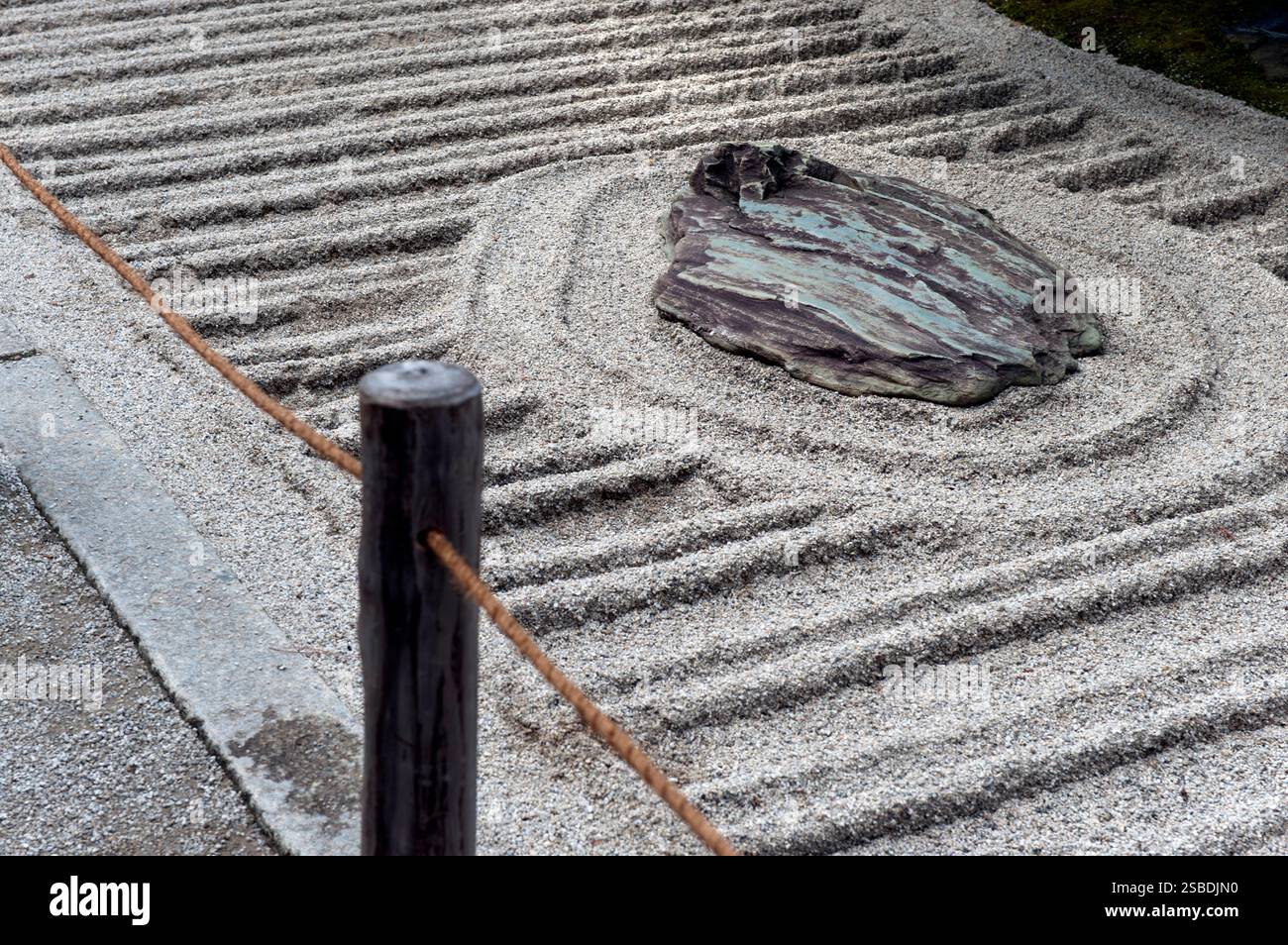 A single rock sits amid a geometric pattern of raked white sand in a ...