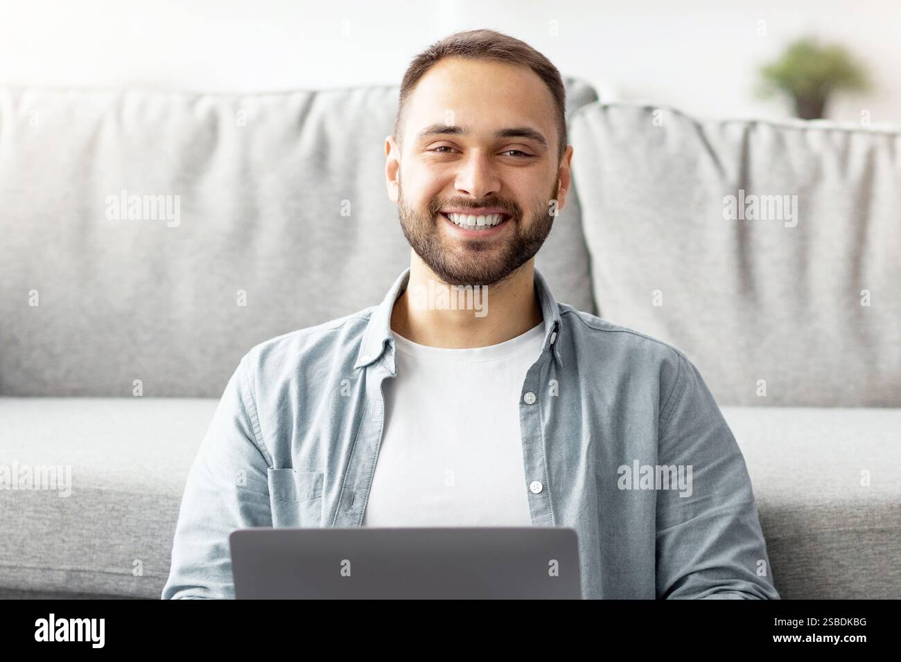 Full length of happy young guy sitting cross legged on floor, using ...