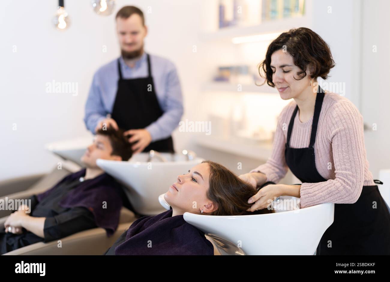 Young woman stylist washes female clients hair, prepares it for cutting ...