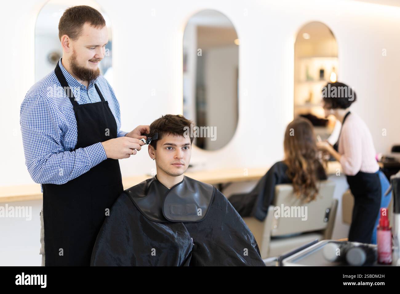 Young man barbershop employee stands next to male client, discussing ...