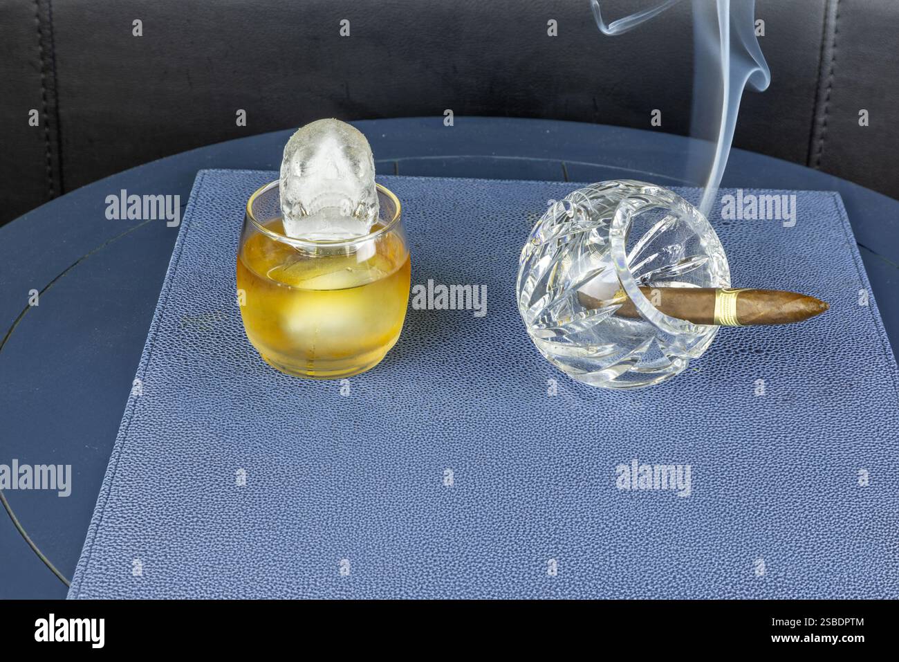 Smoking cigar in a crystal ash tray next to a glass of whisky with an ...