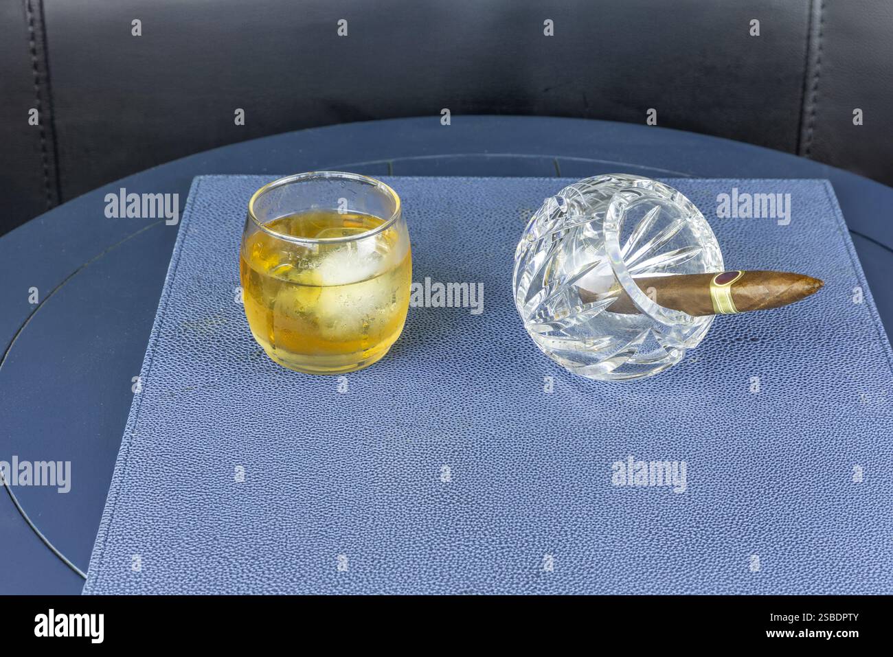 Smoking cigar in a crystal ash tray next to a glass of whisky with an ...