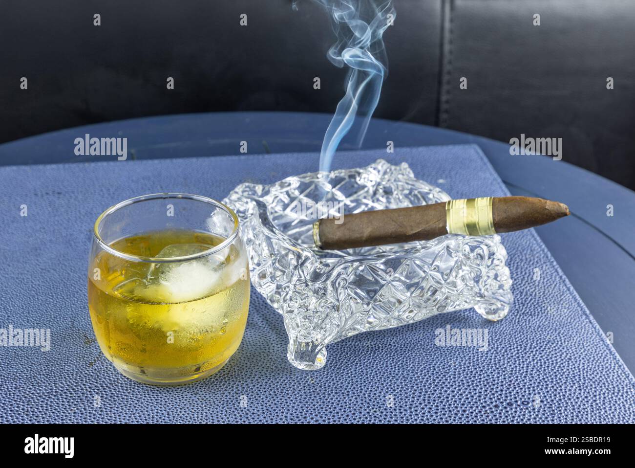 Smoking cigar in a crystal ash tray next to a glass of whisky with an ...