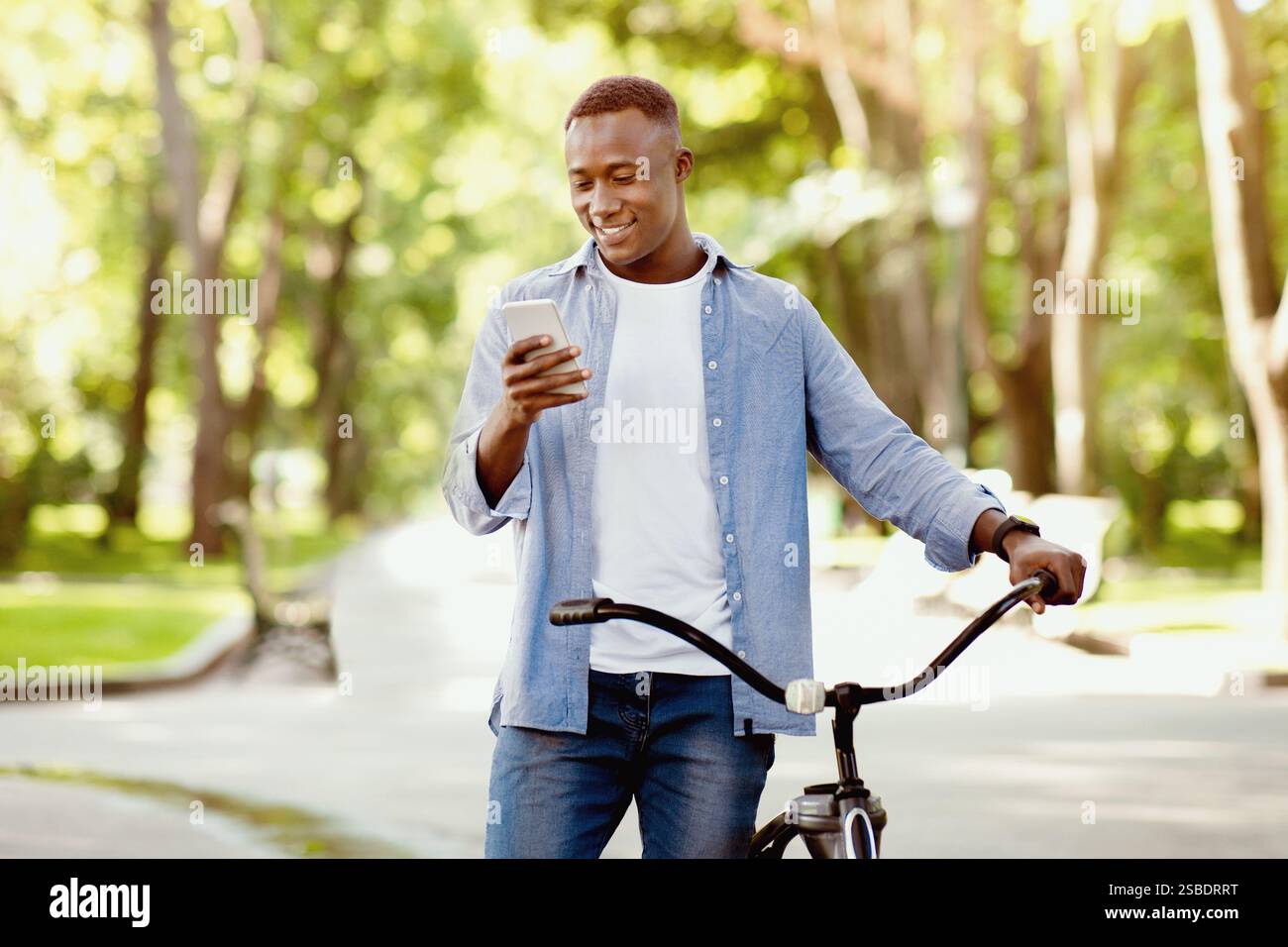 Cool African American guy with modern bike sending message on cellphone ...