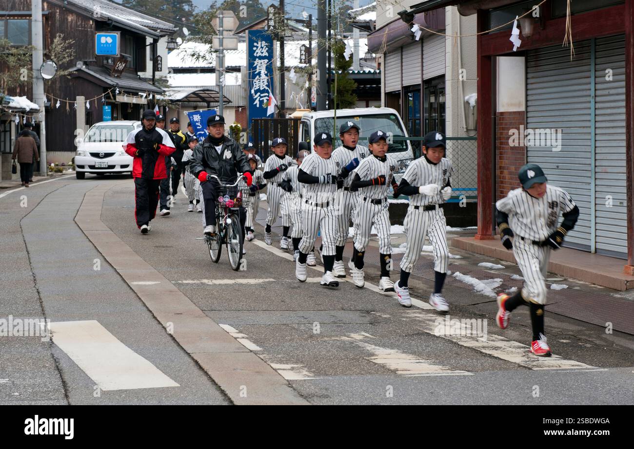 Group of middle school boys in baseball uniforms running along street ...