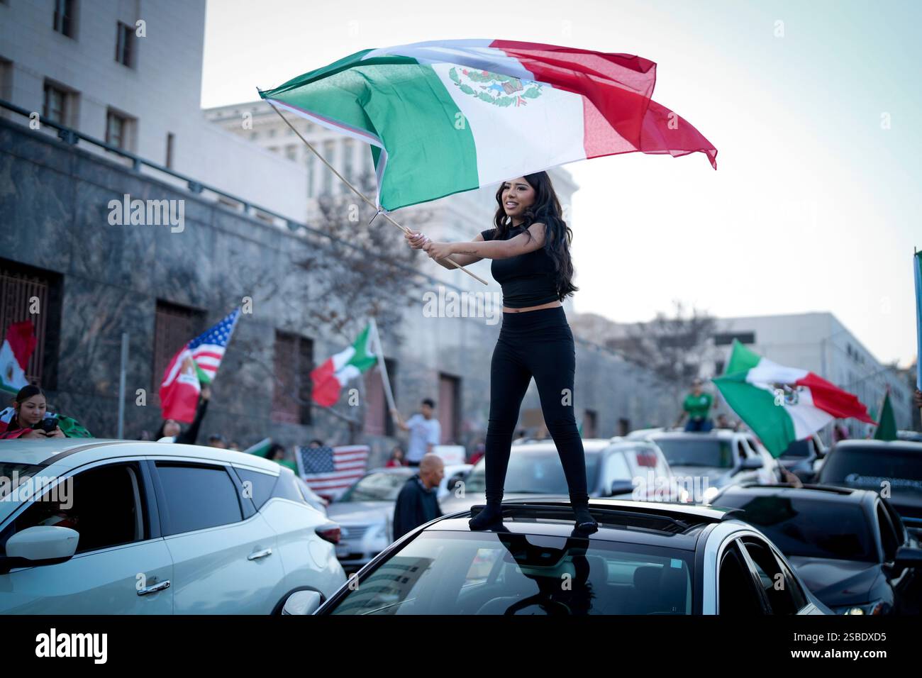 A demonstrator waves a Mexican flag while standing on top of a car ...