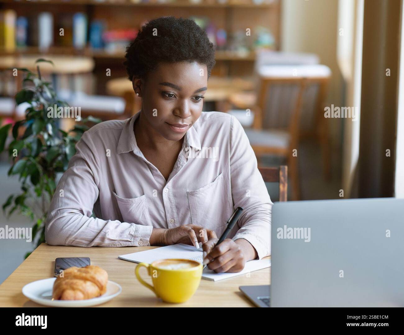 Millennial black woman studying or working online, taking notes in ...