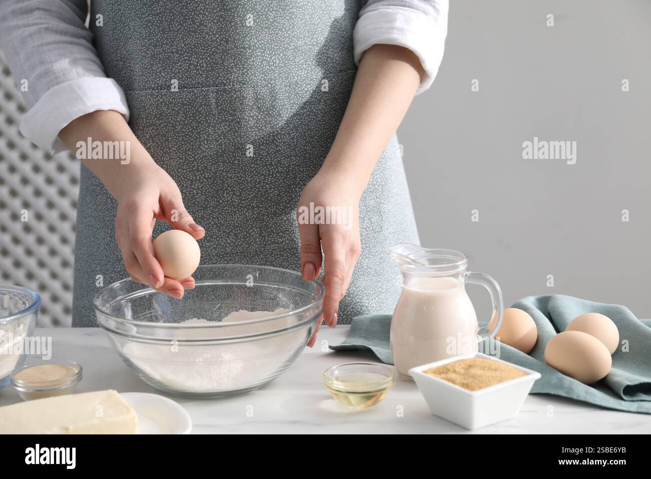Making cinnamon rolls. Woman adding egg into bowl at white marble table, closeup Stock Photo - Alamy