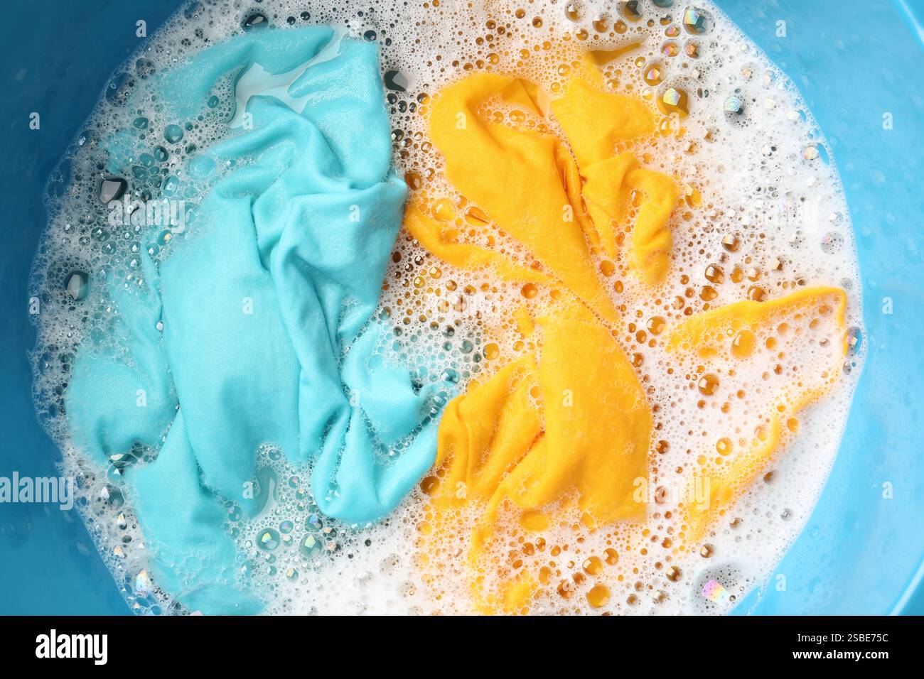 Colorful clothes soaked in water before washing, top view Stock Photo ...