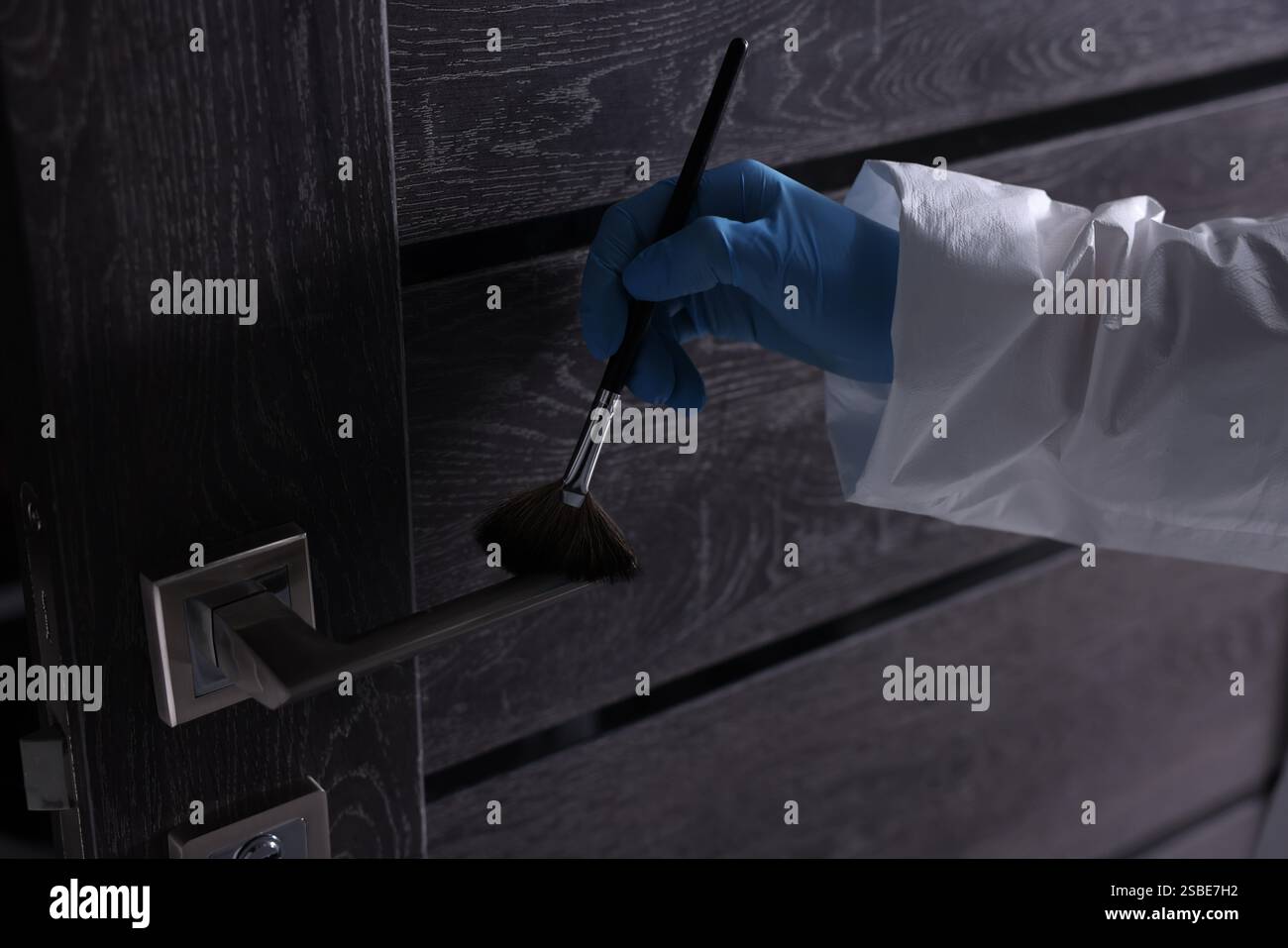 Forensic expert taking fingerprints with brush from handle of door ...