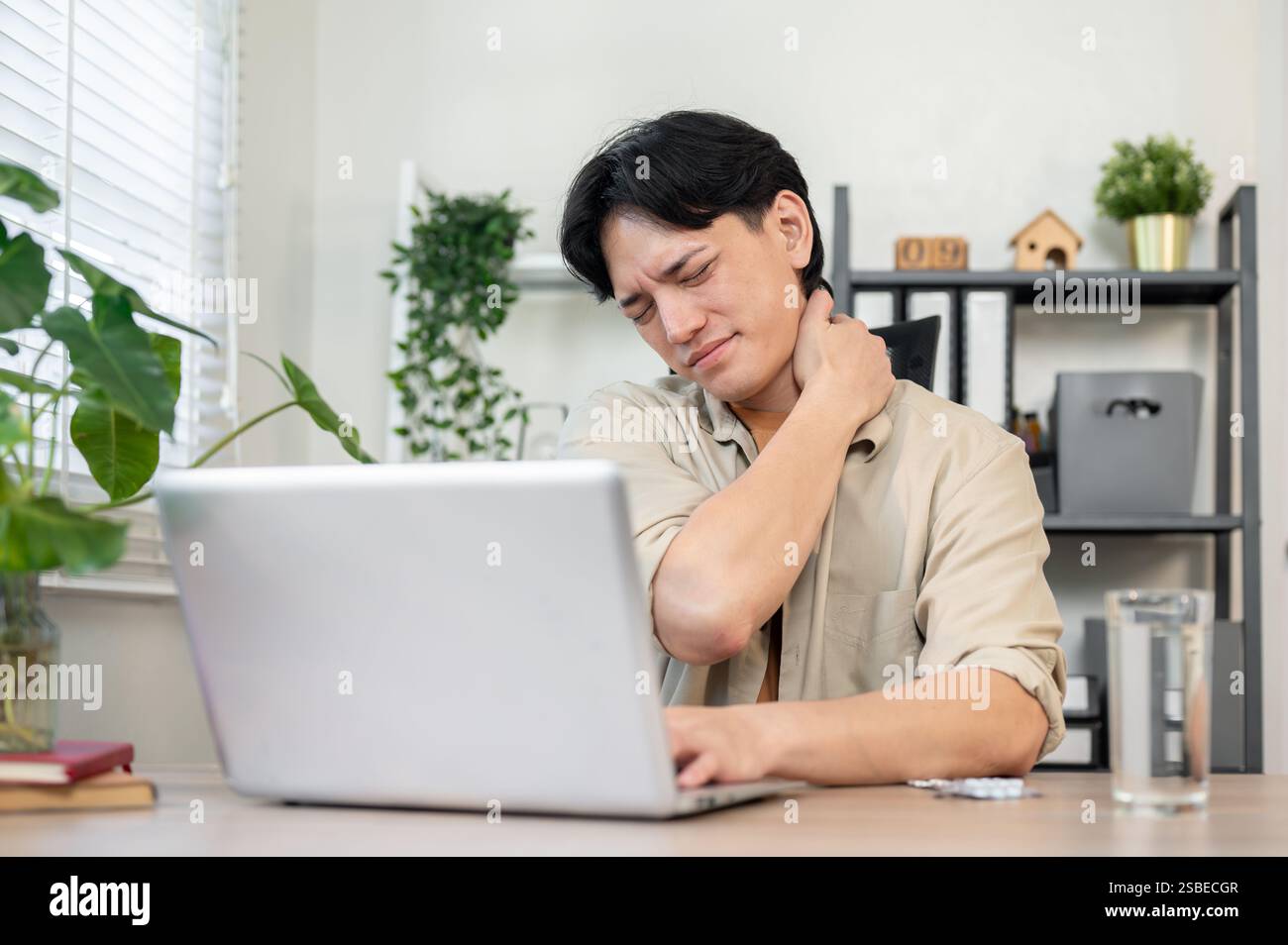 A tired, uncomfortable Asian businessman sits at his desk in front of a ...
