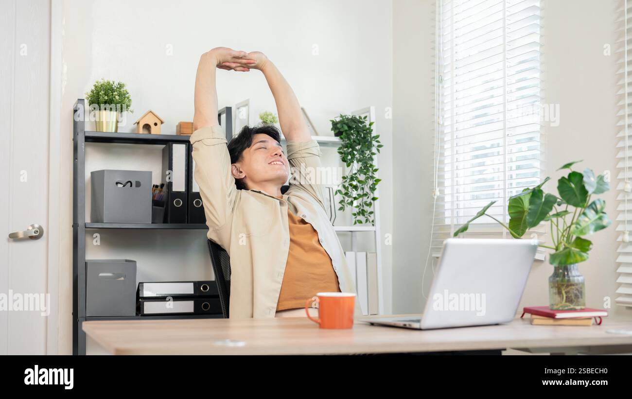 A relaxed, carefree Asian businessman sits at his desk in front of a ...