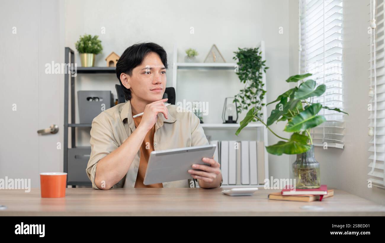 A thoughtful, positive Asian businessman in casual clothes sits at his ...