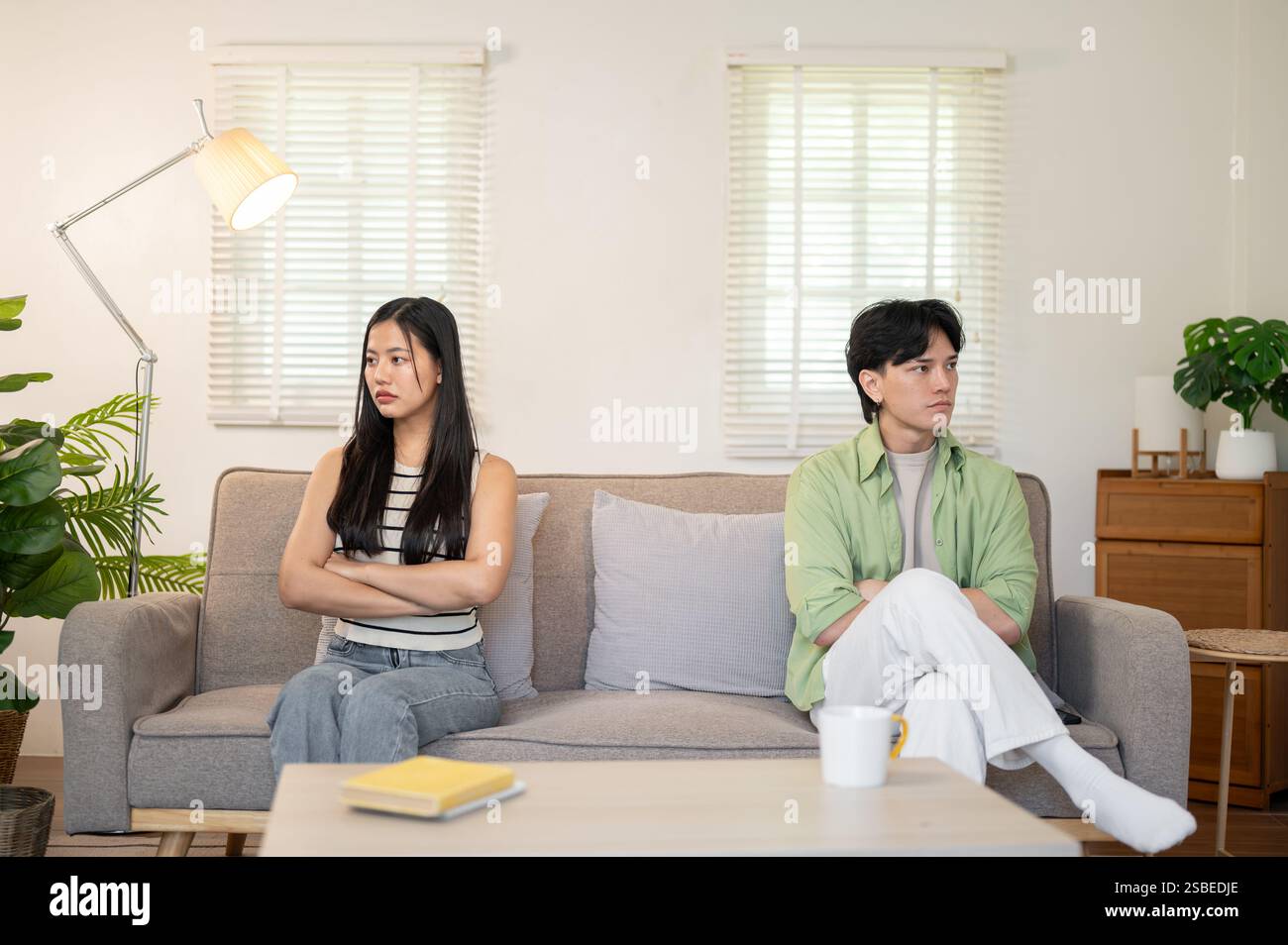 An angry young Asian couple sits separately on the sofa, looking away ...