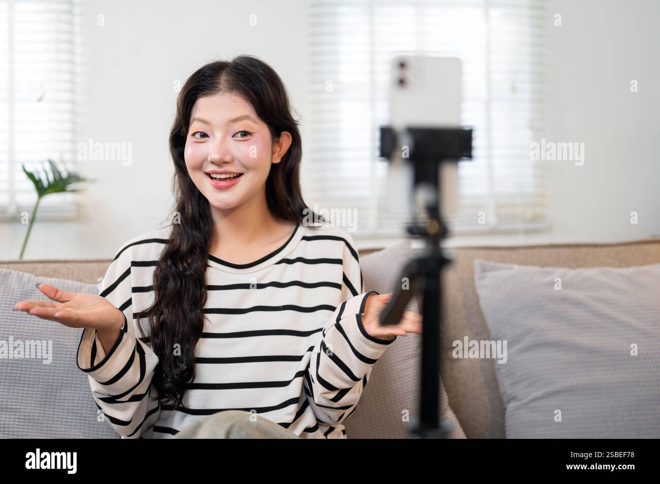 A confident, attractive Asian female influencer sits on a sofa, live ...