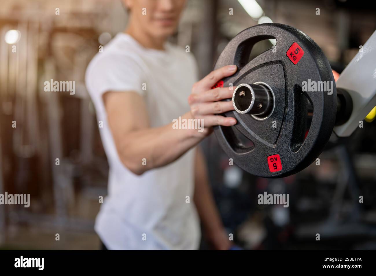 A close-up of a muscular and strong Asian man placing a weight plate on ...