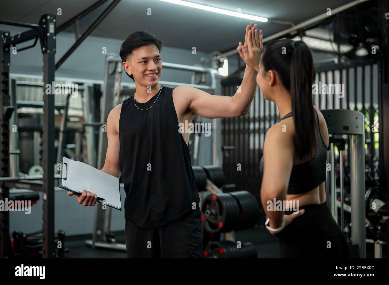 A cheerful, athletic Asian male fitness trainer is giving a high five ...