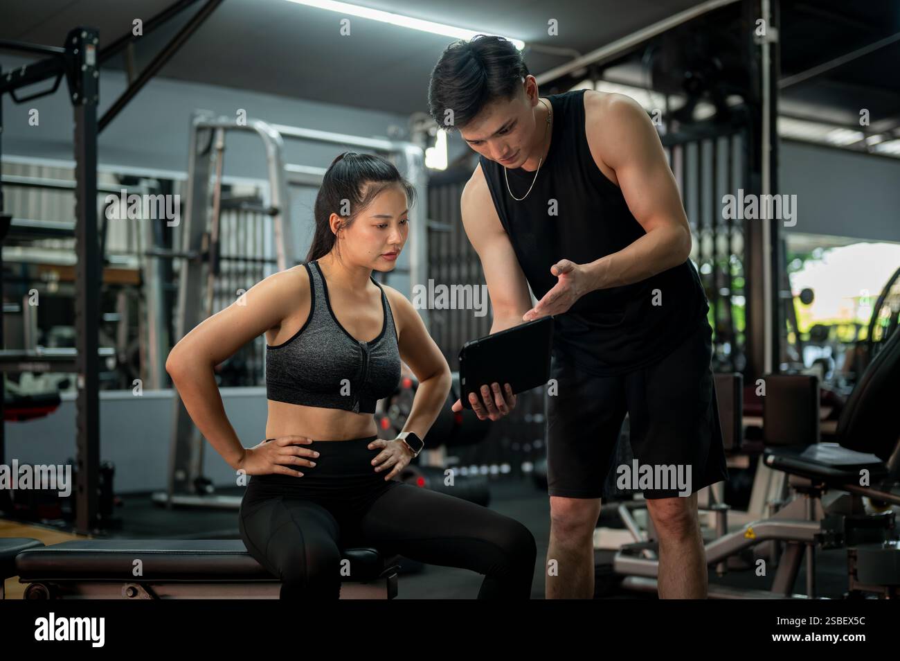 A beautiful and fit Asian female client in sportswear sits on a fitness ...