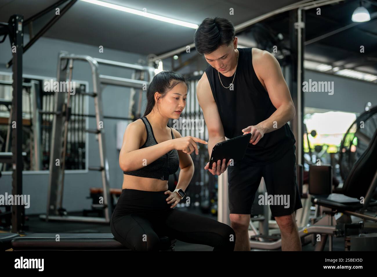 A beautiful and fit Asian female client in sportswear sits on a fitness ...