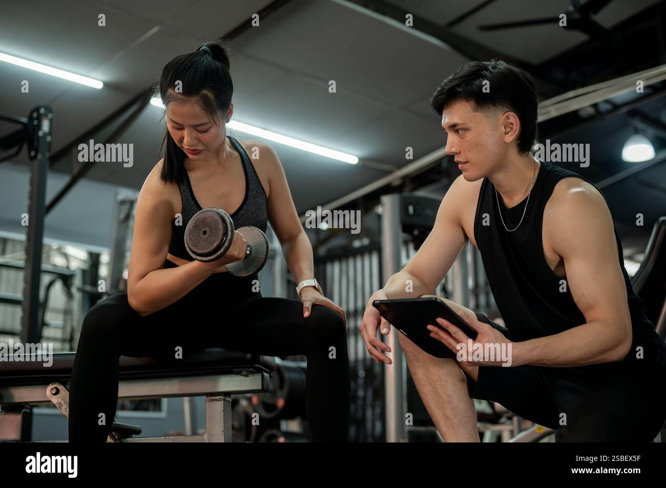 A professional, focused Asian male fitness trainer is supporting and ...