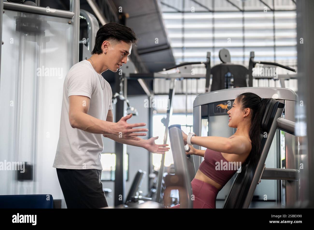 A supportive and professional Asian male fitness trainer is instructing ...