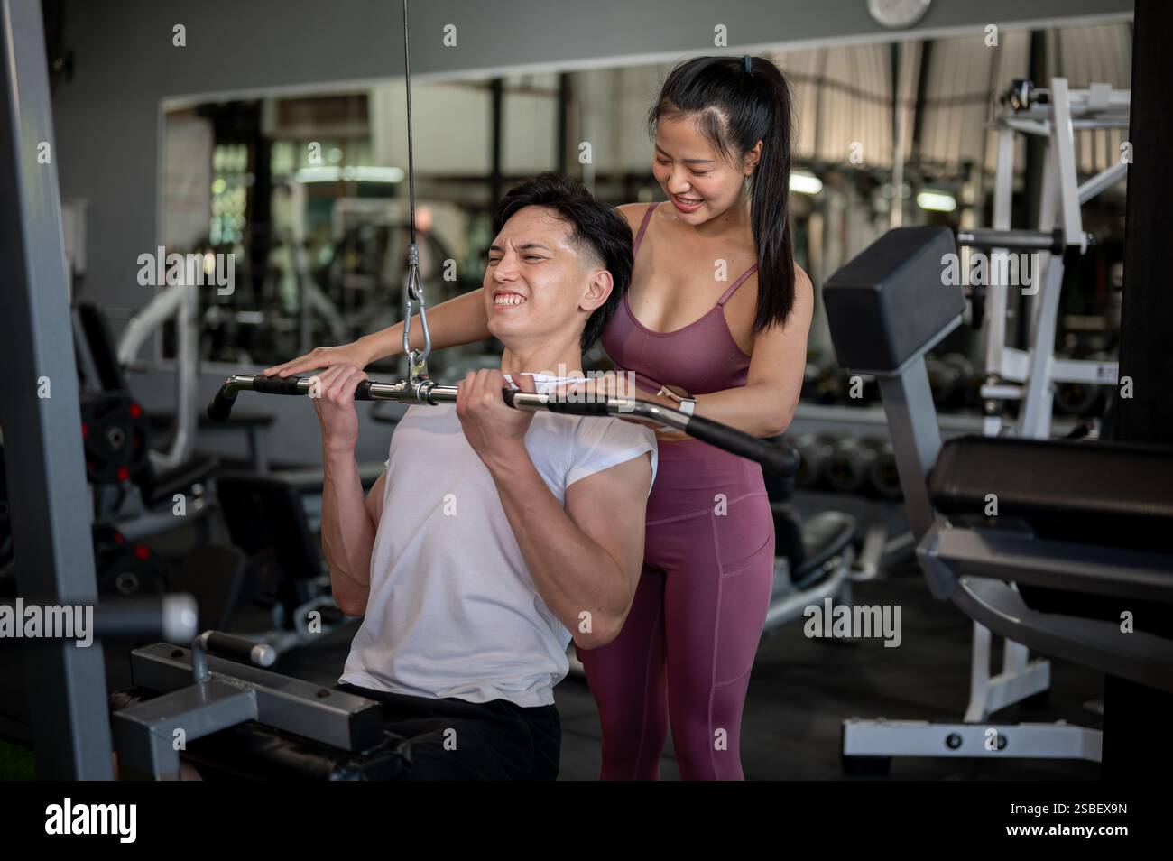 A supportive Asian female fitness trainer is training and instructing a ...