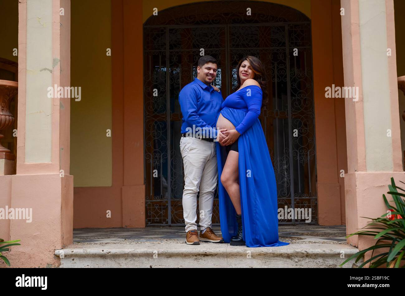 Happy pregnant couple posing in front of a building, touching belly and ...